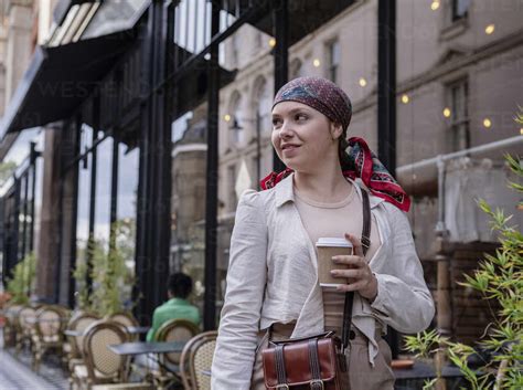 Young Woman Wearing Bandana Holding Disposable Cup At Sidewalk Cafe