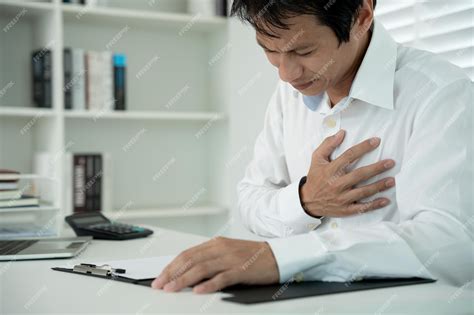 심장마비 증상이 있는 가슴을 손으로 잡고 열심히 일하는 아시아 남성은 심장병 누출 확장으로 인한 가슴 통증이 고통스러운 표정으로