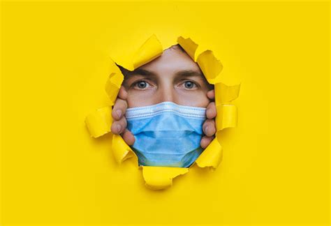 얼굴을 완전히 덮는 보호 의료용 마스크를 착용한 남성이 노란색 종이의 찢어진 구멍을 통해 엿본다 전염병의 개념 격리 및 코로나