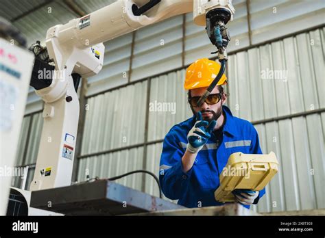 Engineer Controlling Robot Arm At Factory Checking The Operation Of