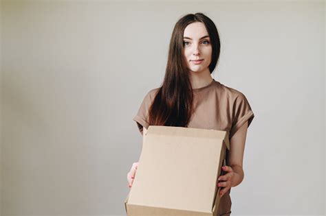 놀란 얼굴과 손에 든 상자를 가진 젊은 여성이 빈 벽에서 카메라를 바라본다 갈색에 대한 스톡 사진 및 기타 이미지 갈색