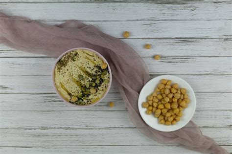 후무스는 흰색 배경과 파스텔 거즈에 분홍색 접시에 유대인 요리의 전통 요리입니다 병아리콩 참깨 페이스트 레몬 씨앗과 크래커로 장식 된 수제 플랫 레이 0명에 대한 스톡 사진