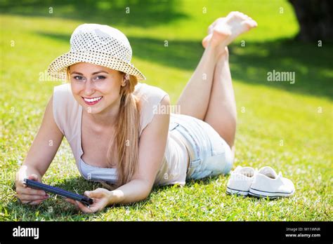 Lächelnden jungen Barfuß liegende Frau auf grünem Gras in Park und Handy in der Hand halten