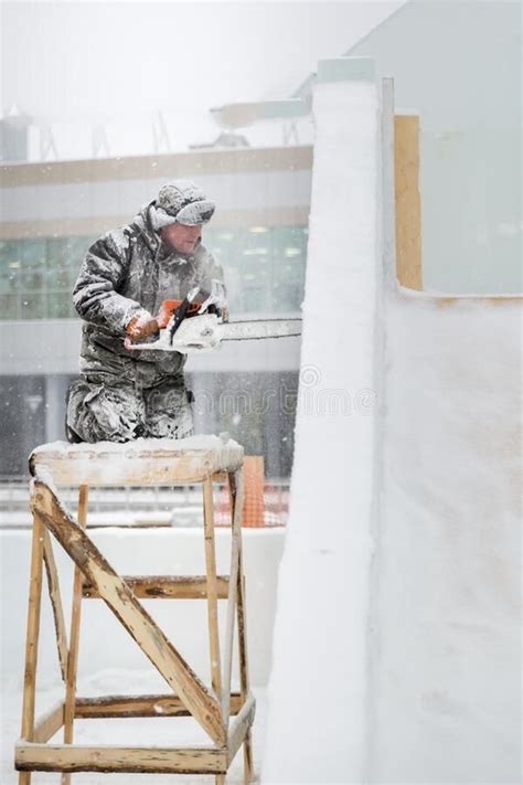 Worker Assembler In A Green Jacket And Black Hat On The Scaffolding