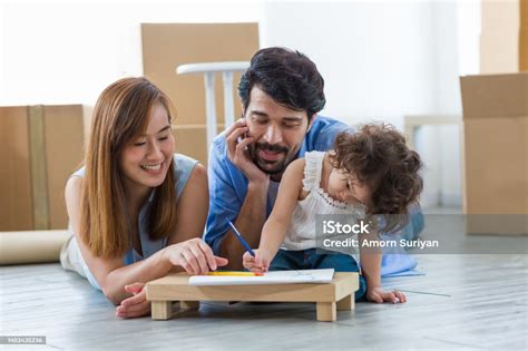 행복한 아버지와 어머니는 바닥에 누워 어린 유아 소녀에게 그림을 그리거나 집에서 색연필로 책을 쓰는 것을 가르칩니다 거실에서