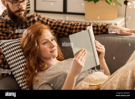 Red Haired Woman Reading A Book And Husband Sitting Behind Her Stock