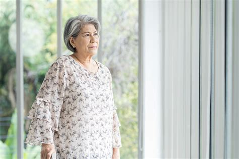 아시아 노인 여성이 병원 창문 근처에 혼자 서 있다 집에서 지팡이를 사용하는 늙은 아시아 여성 은퇴 건강 관리 및 노화 개념