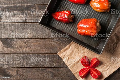 잘라낸 토마토 근처의 직사각형 금속 트레이에 박제 된 후추는 구겨진 종이와 오래된 갈색 소박한 나무 테이블에 놓여 있습니다