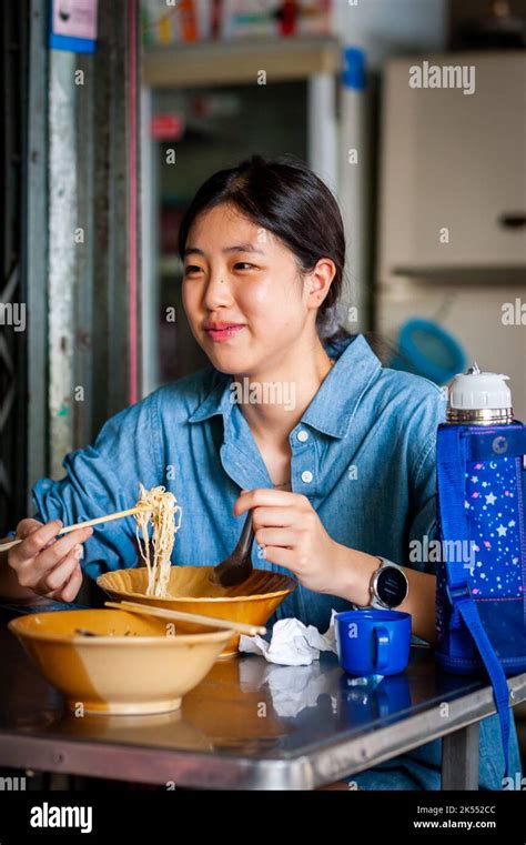 A Young Thai Girl Enjoys Some Noodle Soup In A Street Restaurant In Soi