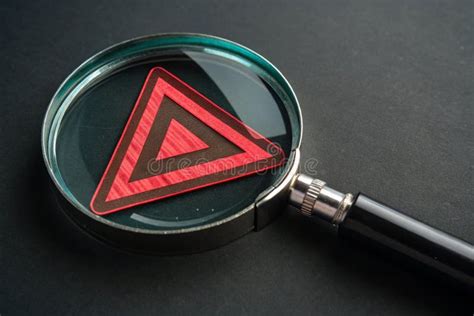 A Red Warning Triangle Inside The Glass Of A Magnifying Glass Against A Black Background With