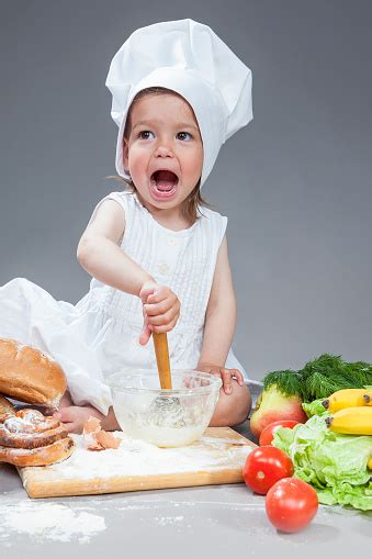 요리 개념 스튜디오 환경에서 거품기와 주방 유리 제품으로 작업 하는 쿡 유니폼에서 백인 어린 소녀를 외치는 초상화 배경에 야채와 과일 수직 샷 2 3 살에 대한 스톡 사진