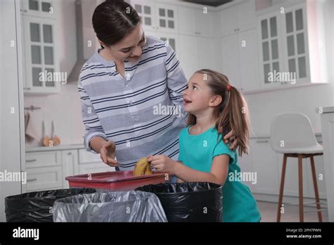Young Woman And Her Daughter Throwing Banana Peel Into Trash Bin In