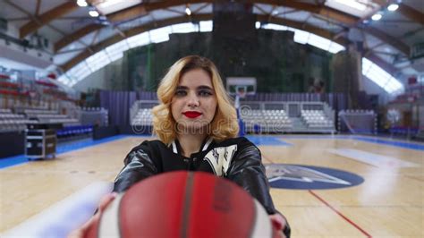 Blond Cheerleader In A Black Jacket Holding A Ball In Front Of A Camera Blurred Foreground