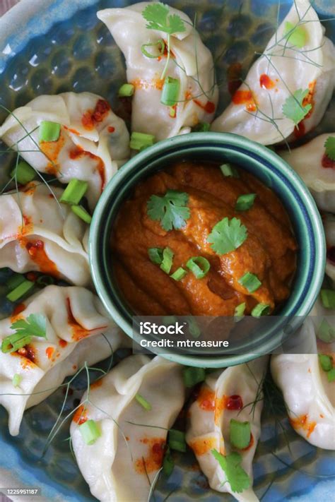 찐 모모 닭고기와 혼합 야채로 채워진 흰 밀가루와 물 반죽 칠리 오일이 뿌려진 오렌지 매운 디핑 소스의 라메킨을 둘러싼 접시에 올려진 모습 높은 전망 중국식 만두에 대한