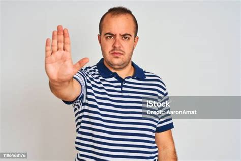 고립 된 흰색 배경 위에 서있는 캐주얼 스트라이프 폴로를 입은 청년은 손바닥으로 노래를 멈추지 않습니다 얼굴에 부정적이고 심각한