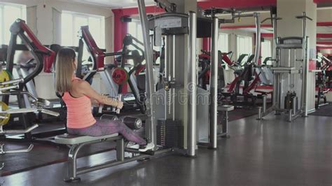 Girl Shakes Her Arm Muscles On Training Simulator In The Gym Or Fitness