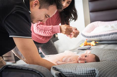 웃는 아버지와 어머니는 침실의 침대에서 카메라를 보고 있는 아기를 입힌다 1개월에 대한 스톡 사진 및 기타 이미지 1개월