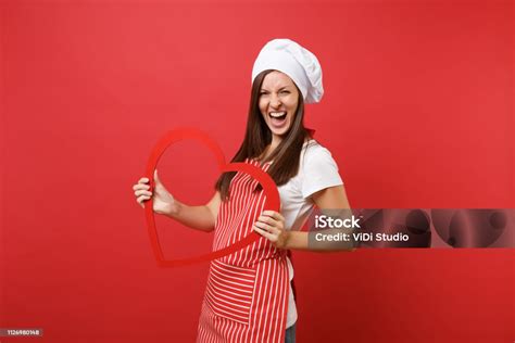 주부 여성 요리사 요리사 또는 줄무늬 앞치마 흰색 티셔츠 모자 요리사 모자 빨간 벽 배경에 고립 된 베이커 가 정부 여 자가