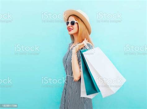여름 밀짚 라운드 모자를 쓰고 쇼핑백을 들고 행복한 미소 짓는 여성 파란색 배경에 검은 색 흰색 줄무늬 드레스 세일에 대한 스톡