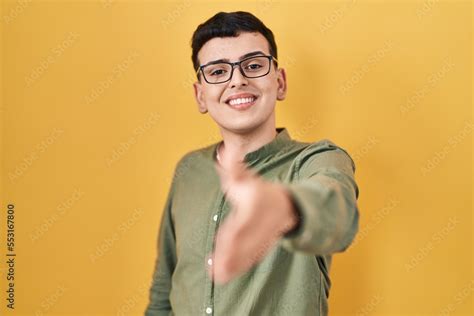 Non Binary Person Standing Over Yellow Background Smiling Friendly Offering Handshake As