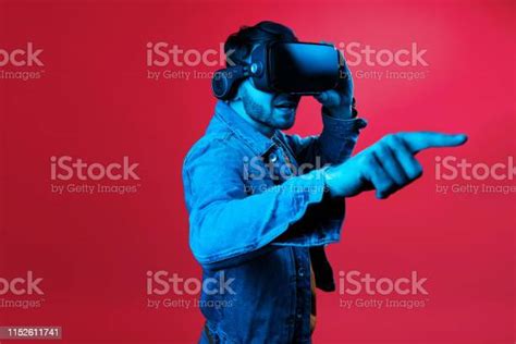 네온 빛에 빨간색 배경에 스튜디오에서 가상 현실 고글을 입고 젊은 잘생긴 수염 남자 Vr 헤드셋을 사용 하 여 스마트 폰 3차원 형태에 대한 스톡 사진 및 기타 이미지