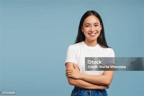팔짱을 끼고 포즈를 취하는 웃는 아시아 여성이 파란색 배경에 카메라를 보고 있습니다 여자에 대한 스톡 사진 및 기타 이미지