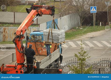Workers With The Help Of A Truck Crane Unload A Truck With Road Tiles