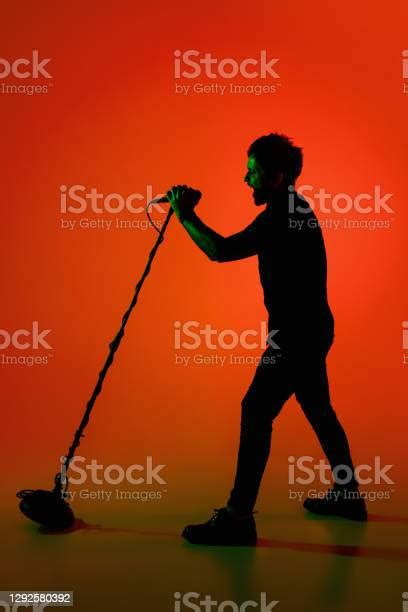 네온 빛에 오렌지 그라데이션 스튜디오 배경에 고립 된 젊은 백인 남성 가수의 실루엣 25 29세에 대한 스톡 사진 및 기타