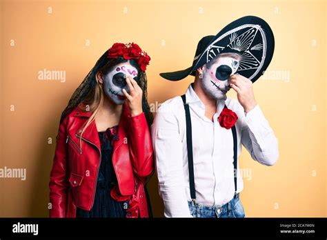 Couple Wearing Day Of The Dead Costume Over Yellow Tired Rubbing Nose