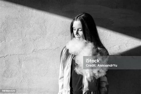 Vape 십대 캐주얼 한 옷을 입은 어린 귀여운 소녀가 여름날 야외 벽 근처에서 전자 담배를 피울 수 있습니다 건강에 해로운