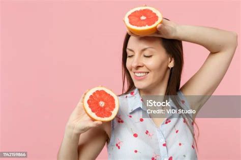 여름 옷에 예쁜 젊은 여 자가 눈을 감고 분홍색 파스텔 배경에 고립 된 신선한 익은 자 몽의 절반을 유지 사람들은 생생한 라이프 스타일 휴식 휴가 개념입니다 복사 공간을