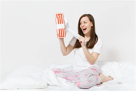 빨간 줄무늬 선물 상자 흰색 시트 베개 담요 흰색 배경에 고립에 배치와 함께 침대에 앉아 젊은 갈색 머리 여자 행복 한 여자