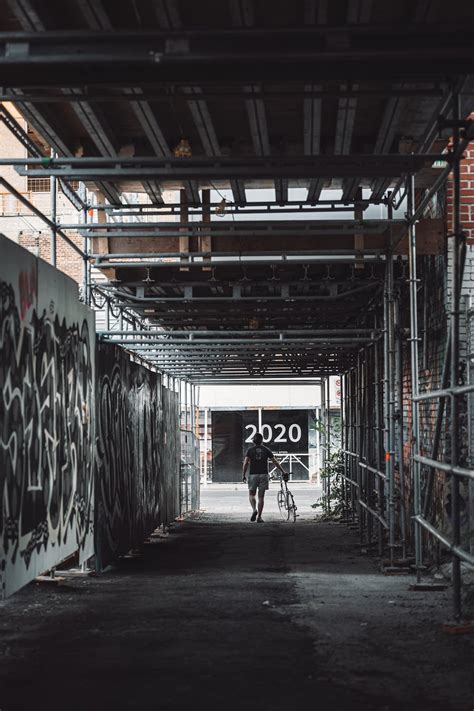 A Person Walking With His Bicycle Under A Steel Scaffolding · Free