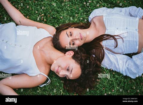 Two Relaxed Girls Laying Down On The Grass In A Park While They Are