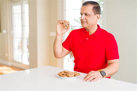 똑똑한 얼굴에 자신감 있는 표정으로 집에서 초콜릿 칩 쿠키를 먹는 중 령 남자 진지한 생각 감정에 대한 스톡 사진 및 기타 이미지 감정 남자 남자들만 Istock