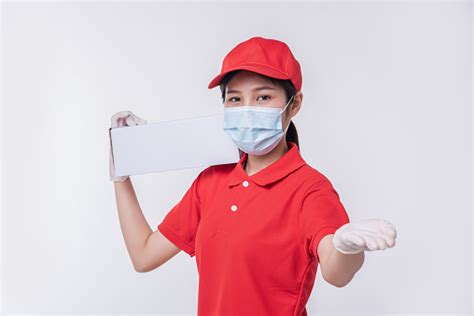 빨간 모자 빈 티셔츠 유니폼 얼굴 마스크 장갑을 낀 의식이 있는 젊은 배달원의 이미지는 밝은 회색 배경 스튜디오에 격리된 빈