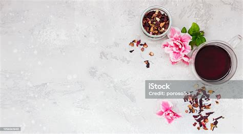 분홍색 꽃과 밝은 회색 콘크리트 배경에 마른 차 잎 유리 머그잔에 뜨거운 히비스커스 차와 구성 복사 공간이 있는 상단 뷰입니다