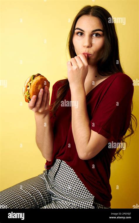 Woman Licking Her Fingers After Taking A Bite Of A Hamburger In Her