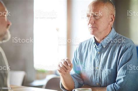 블루 셔츠 테이블에 앉아 하 고 현대적인 카페에서 친구와 의사 소통에 심각한 잠겨있는 잘생긴 성숙한 남자 남자에 대한 스톡 사진
