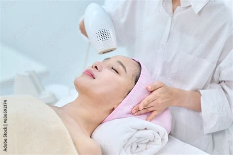 Foto De 아시아 한국의 젊은 여성이 스파 또는 피부관리전문점 또는 피부과 병원에서 분홍색 두건을 쓰고 침대에 누워 베이지색