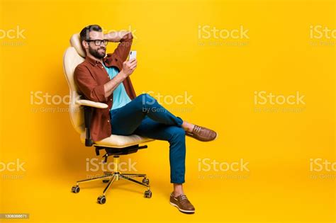 스마트폰 소셜 미디어가 의자에 앉아 있는 모습은 생생한 노란색 배경이 된 미소 짓는 프리랜서의 전신 사진 앉음에 대한 스톡 사진