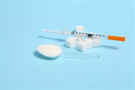 투명 측정 숟가락에 흩어져 흰색 설탕의 상단 보기와 파란색 배경에 흰색 순수 정제 설탕 큐브에 인슐린 주사기 과도한 백색 설탕