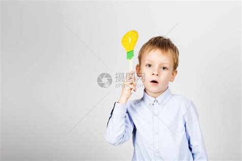 有黄色纸电灯泡的逗人喜爱的男孩反对白色背景拿着玩具灯泡的小学生快乐微笑的孩子与有趣的照片道具学校理高清图片下载 正版图片502910606 摄图网