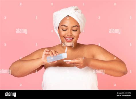 Beautiful Black Chubby Woman Applying Lotion On Cotton Pad Over Pink