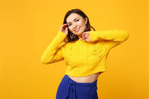 스웨터에 즐거운 젊은 여자의 초상화 파란색 바지 카메라를 찾고 노란 오렌지 배경에 고립 된 얼굴 가까이 손을 유지 사람들은