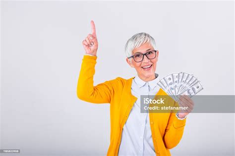 현금을 많이 들고 행복 한 수석 여자 흰색 배경에 백 달러 지폐와 노인 여자와 그녀의 손가락으로 가리키는 100 달러 지폐 미국