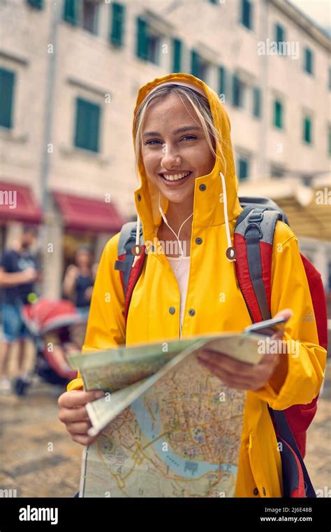 Young Smiling Girl With A Yellow Raincoat And Map On The Street While