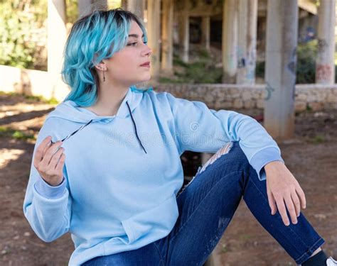 Blue Haired Teenage Girl In Light Blue Oversize Hoodie Sitting Under