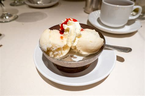 반짝이는 금속 그릇에는 휘핑크림을 얹고 생생한 딸기 소스를 뿌린 크리미한 바닐라 아이스크림 두 스쿱이 우아한 식기와 함께 산뜻한