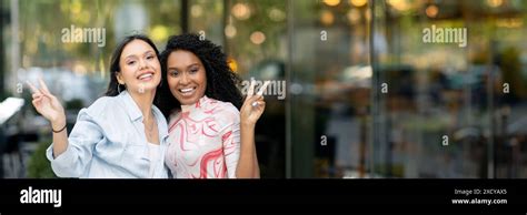 Two Cheerful Girlfriends Posing Outside Together Showing Peace